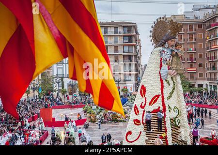 Woman placing flower offerings on large wooden replica statue of Virgen ...