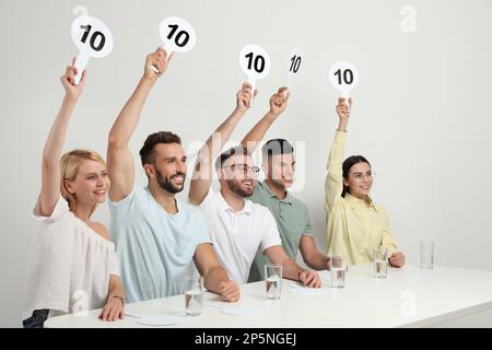 Panel of judges holding signs with highest score at table on white ...