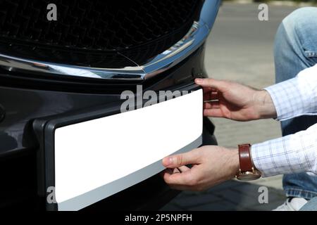 Man installing vehicle registration plate outdoors, closeup. Mockup for ...