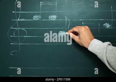 Teacher writing music notes with chalk on greenboard, closeup Stock ...