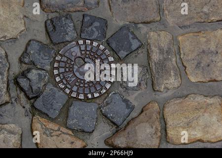 Round metal hatch in urban pavement, sewer manhole cover with yellow ...