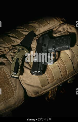 A small modern pistol and penknife on a brown military backpack. Self ...