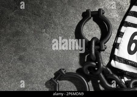 Steel shackles and jail clothes on grey table, flat lay. Space for text ...