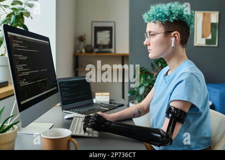 Young IT specialist with prosthetic arm concentrating on her online work, she working with ...