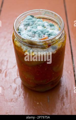 Mold on red jam. Spoiled product in a glass jar. Green and white fungi ...