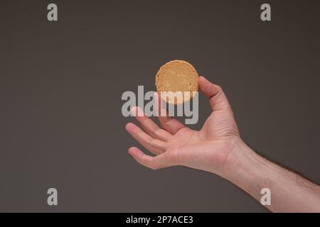 Single shortbread biscuit held by male hand. Close up studio shot ...