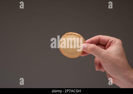 Single shortbread biscuit held by male hand. Close up studio shot ...