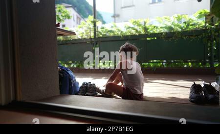 One small boy putting shoes on by doorstep ready to go out. Kid getting ...