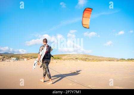Portrait wave kitesurfer walking upwind at beach with his board and ...