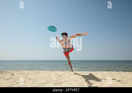 Sportive man jumping while trying to catch flying disk at beach Stock ...