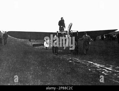 Pilot Louis Bleriot stands in the cockpit of his plane while mechanics ...