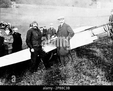 Pilot Louis Bleriot stands in the cockpit of his plane while mechanics ...
