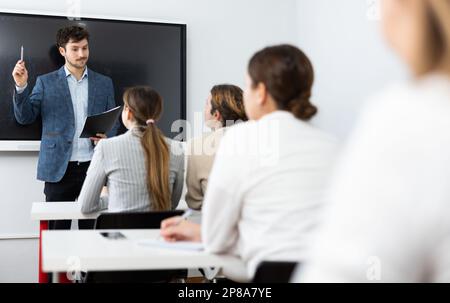 Positive male trainer, conducting advanced training courses to office employees sitting at desks ...