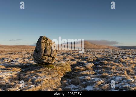 A large boulder stands on limestone pavement, with a view of Whernside ...