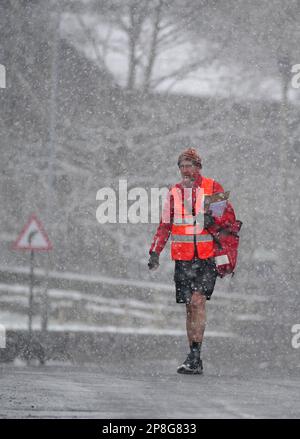 A postal delivery worker wearing shorts in heavy snow fall during his ...