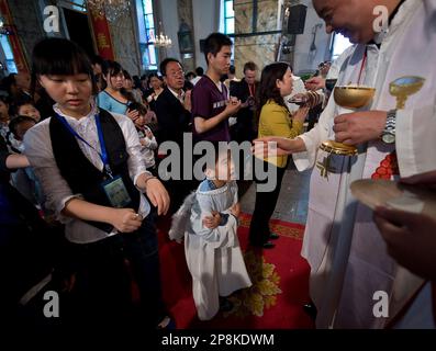 Chinese Catholics line up to receive bread from a priest outside the ...