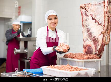 Young female butcher showing how minced meat is prepared in butchery ...