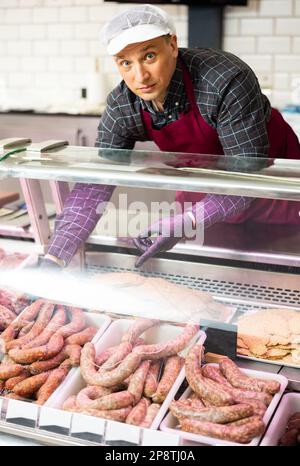 Butcher offering fresh raw sausages displayed in glass showcase Stock ...