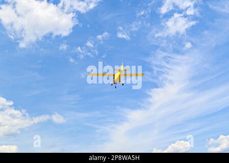Yellow single-engine ultralight airplane flying in the blue sky with ...