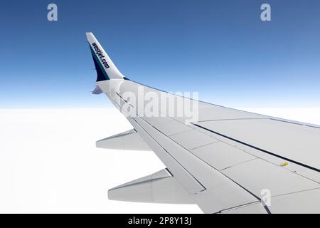 Looking at an airborne WestJet passenger jet wing against blue sky and ...
