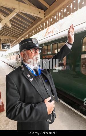 Train guard signalling the departure of historic train on the Keighley ...