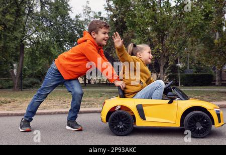 Cute boy pushing children's car with little girl near fountain on city ...