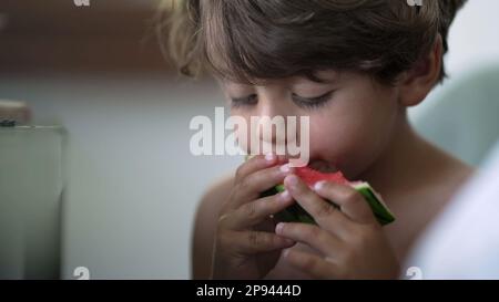 Candid child taking a bite of red watermelon fruit. One small boy ...