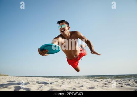 Sportive man jumping and catching flying disk at beach Stock Photo - Alamy