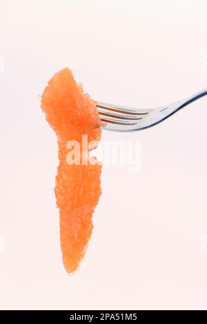 A single segment of grapefruit on a fork for ready to eat against a ...