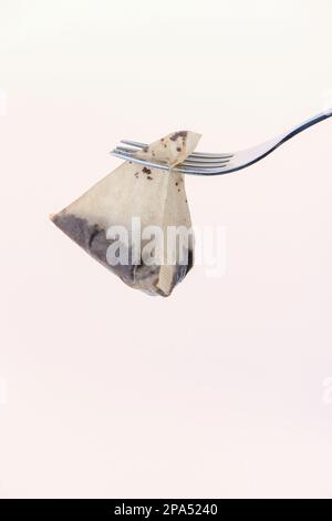 Used triangle tea Bag hanging from a fork against a white background ...