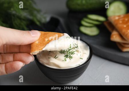 Woman dipping cracker into tasty creamy dill sauce at black wooden ...