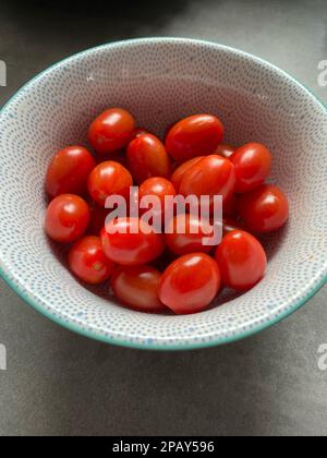 Small red Roma tomatoes in a green glass bowl on a white background ...