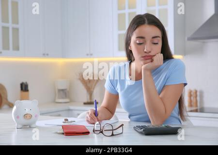 Sad young woman counting coins at table Stock Photo - Alamy