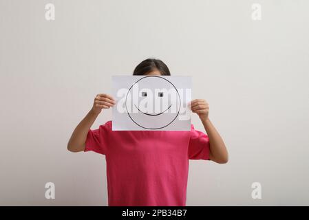 Little girl hiding behind sheet of paper with laughing face in ...