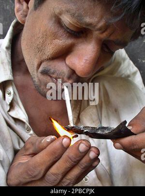 A Pakistani drug addict smokes heroin on the side of the road in ...
