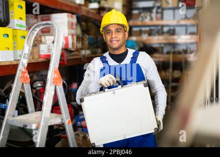 Smiling latin american foreman standing with tool case in store Stock ...