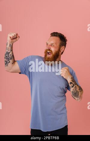 Ginger white man screaming and making winner gesture isolated over pink ...