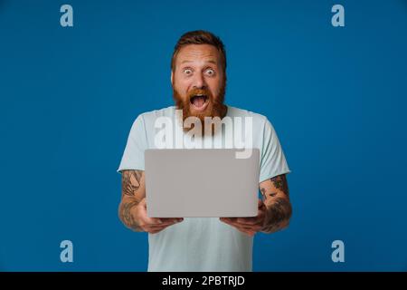 Ginger excited man with tattoo screaming and working with laptop ...