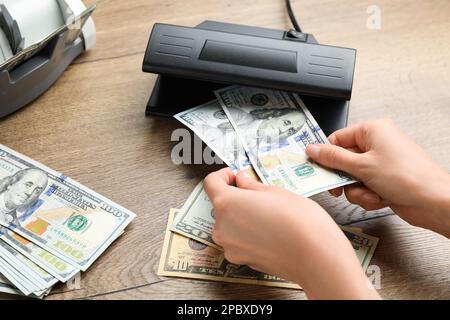 Woman checking dollar banknotes with currency detector on white ...