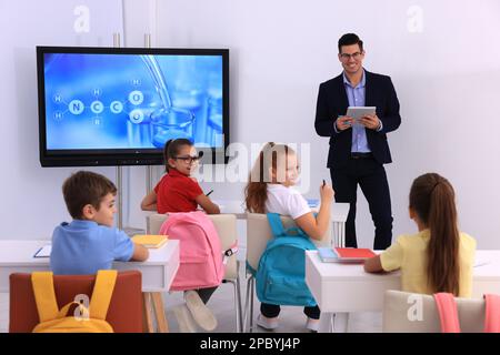 Teacher giving lesson to pupils near interactive board in classroom ...