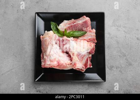 Plate with raw chopped meaty bones on grey table, top view. Space for ...