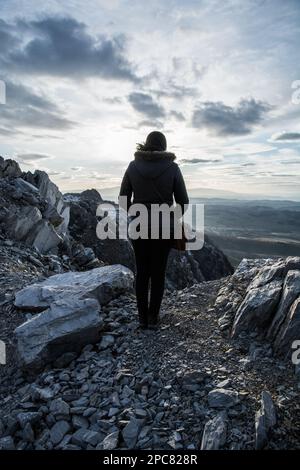 Woman stands on rocky cliff overlooking expansive canyon landscape on a ...