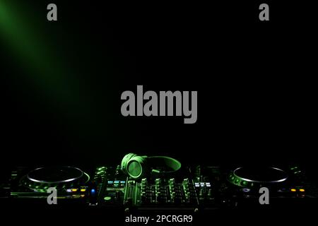 Modern DJ controller and headphones under beam of light on black ...