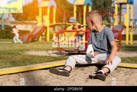 crying child with broken limb arm sits outdoors and looking how kid ...