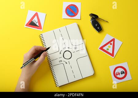 Woman with workbook for driving lessons and road signs at wooden table ...