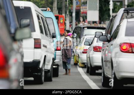 A poor Filipino woman begs along a street in suburban Manila ...