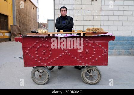 An Uyghur man selling traditional nuts candies from his mobile cart in ...