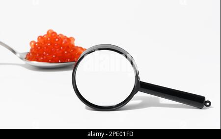 Magnifying glass and spoon with red caviar on a white background Stock ...