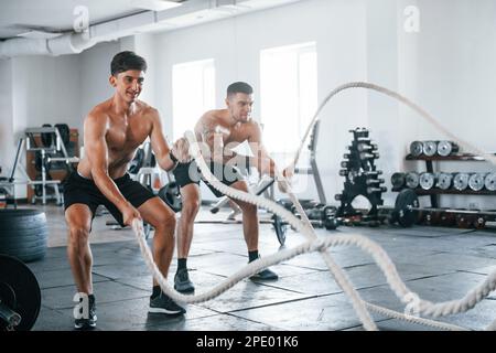 Young people with sportive body shapes doing crossfit by using knots ...