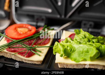 A sandwich maker with two different sandwiches with tomatoes, ham ...
